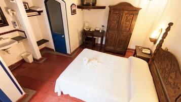 Quarto de hotel com cama, secretária, guarda-roupa, televisão, telefone e banheiro.