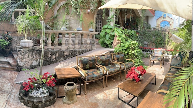 Um pátio externo com piso de pedra, móveis de madeira e plantas em vasos.