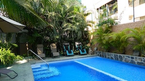 Piscina com espreguiçadeiras, cercada por vegetação exuberante e um muro de pedra.