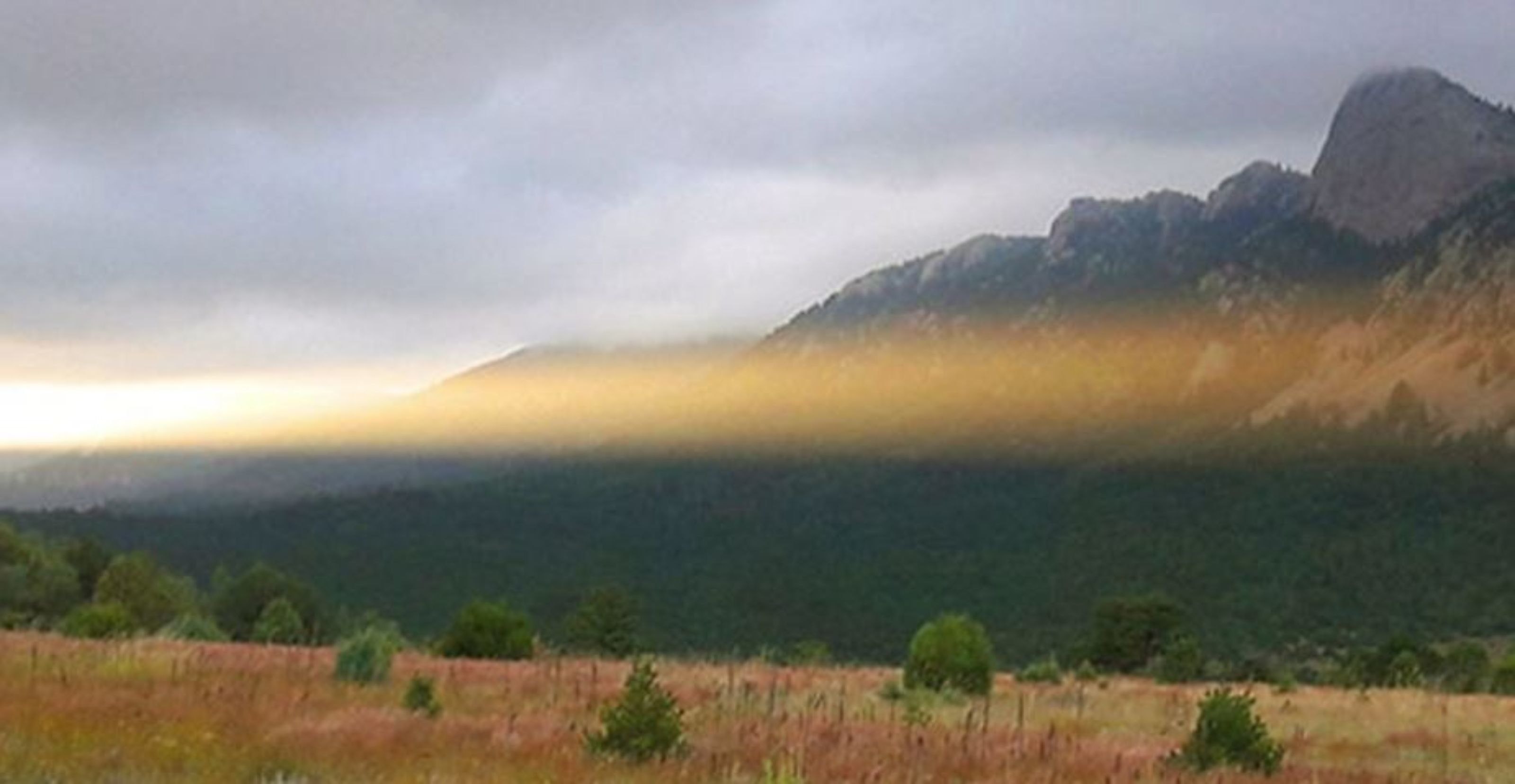 Paisagem montanhosa com um campo em primeiro plano e uma cordilheira ao fundo.