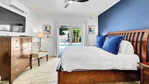 Quarto com cama, cômoda de madeira, ventilador de teto e vista para o exterior.