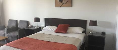 Quarto de hotel com cama, duas mesas de cabeceira, uma cadeira e um abajur.