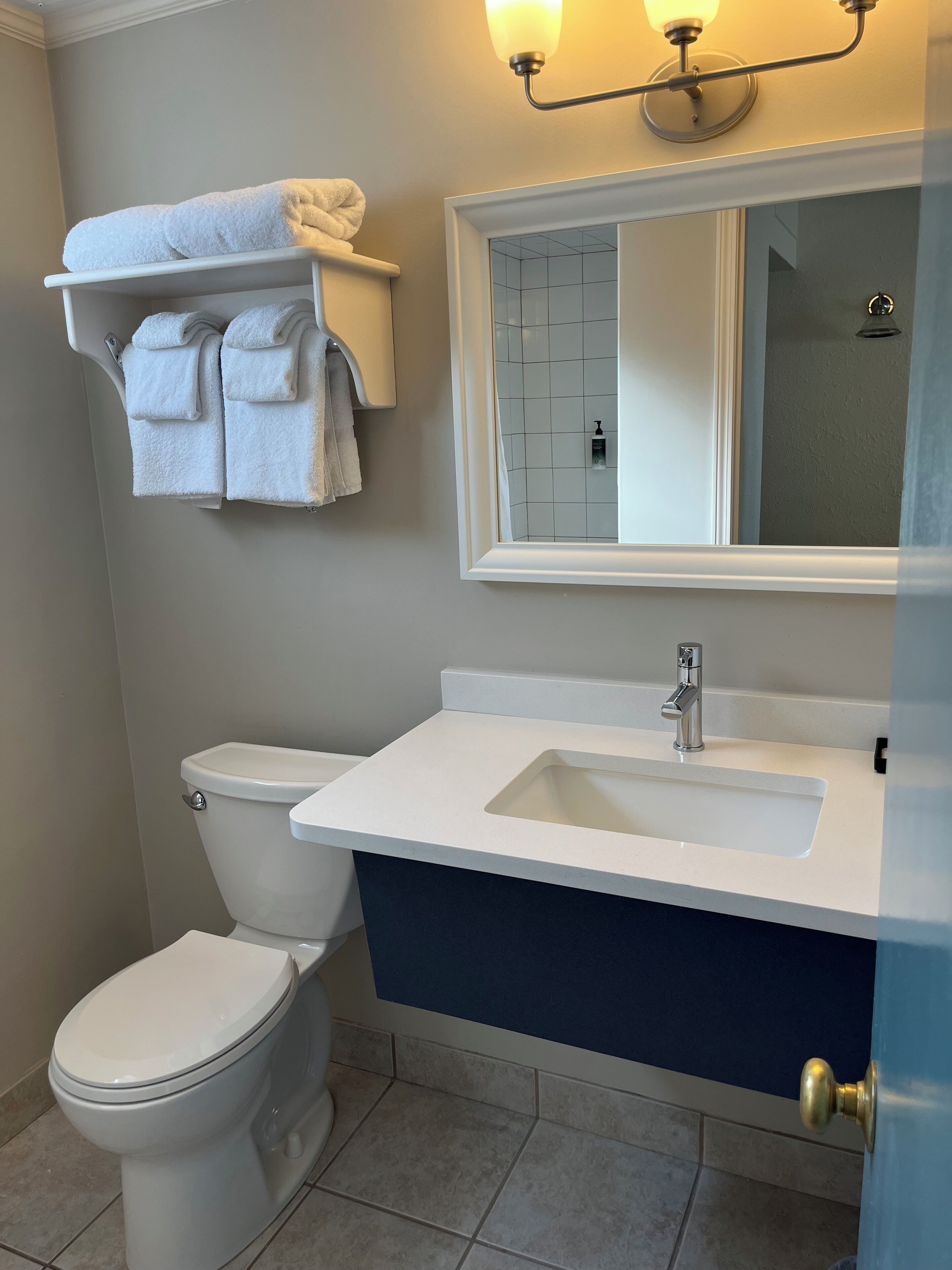 Casa de banho com sanita branca, lavatório branco com bancada azul e espelho sobre o lavatório.