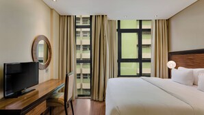 Quarto de hotel com cama, televisão, secretária e janela com cortinas.
