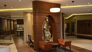 Um saguão com uma estátua, cadeiras estampadas e um lustre moderno.