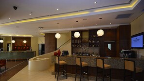 Uma área de bar com balcão curvo, banquetas e uma tela de exibição.