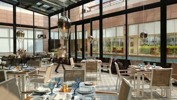 Restaurante moderno com paredes de vidro, mesas bem arrumadas e luminárias pendentes.