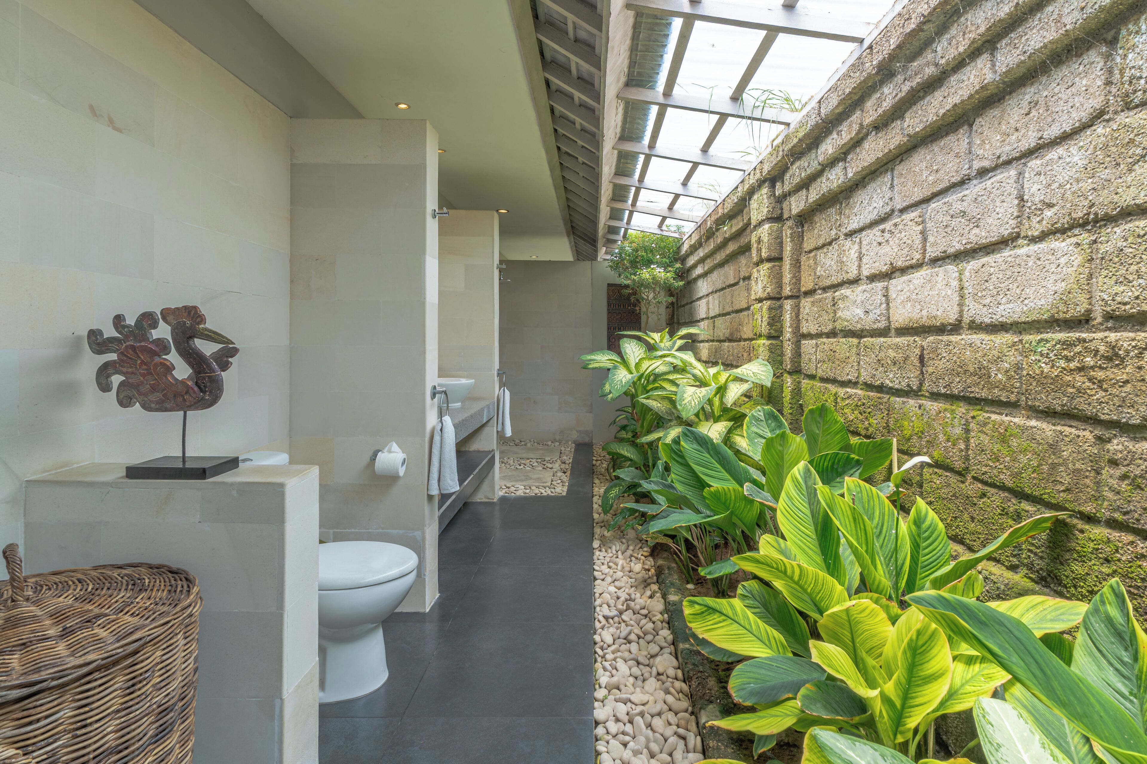 Casa de banho moderna com sanita branca, lavatório e chuveiro. Há uma escultura decorativa na parede e uma cesta no chão.