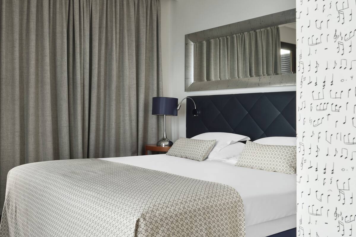Quarto de hotel com uma cama grande, mesa de cabeceira, abajur e espelho sobre a cama.