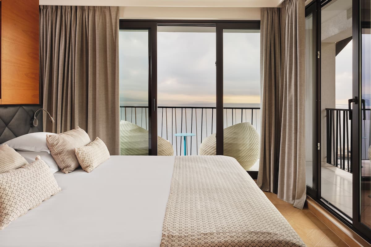 Quarto de hotel com uma cama grande, varanda com vista e porta de vidro deslizante.