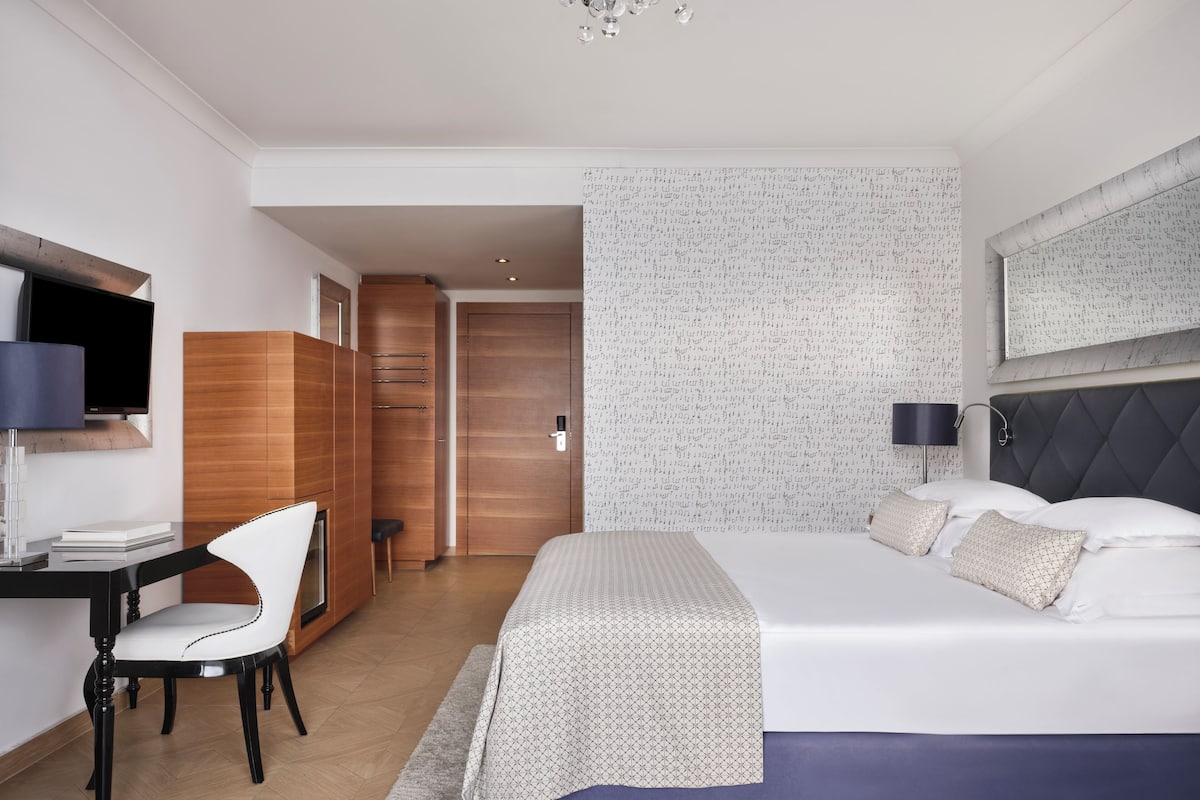 Quarto de hotel moderno com uma cama, uma escrivaninha, uma cadeira e um guarda-roupa.