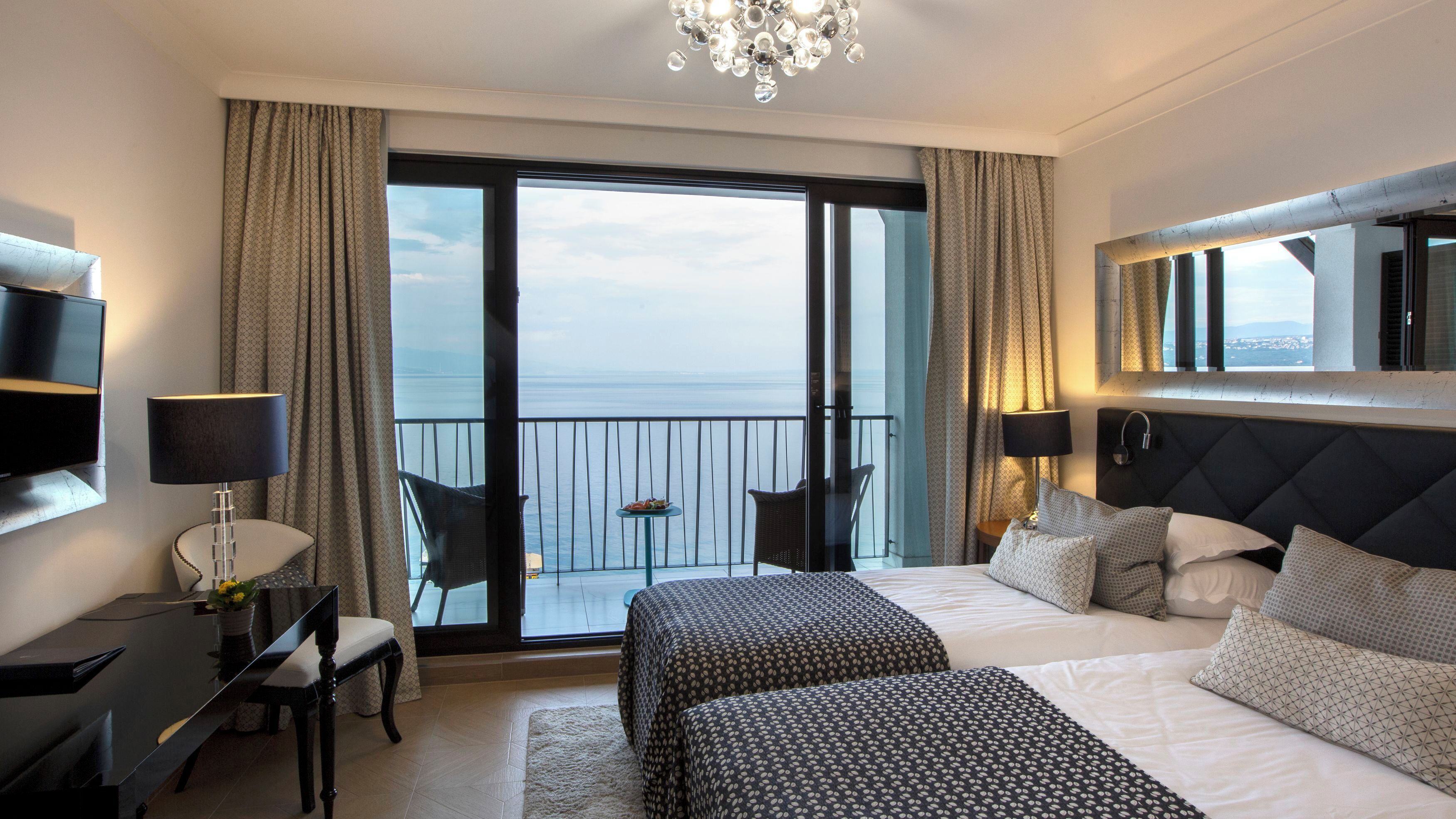 Quarto de hotel com cama, escrivaninha, cadeira, televisão e varanda com vista para o mar.