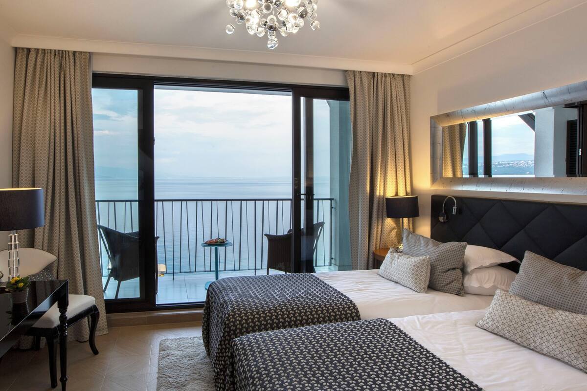 Quarto de hotel com cama, escrivaninha, cadeira, televisão e varanda com vista para o mar.