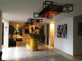 Um hall amplo com piso de azulejos, um grande cachepot amarelo e uma escada com corrimão geométrico.