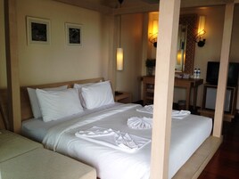 Quarto de hotel com uma cama grande, mesa de cabeceira, espelho, televisão e pequeno frigorífico.