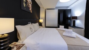 Quarto de hotel com uma cama grande, duas mesas de cabeceira, uma televisão de tela plana e um quadro na parede.