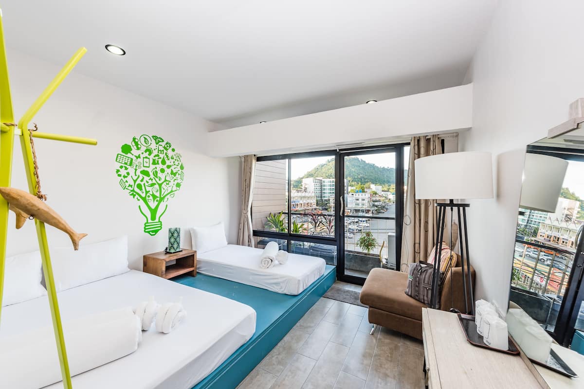 Quarto de hotel moderno com cama, sofá, escrivaninha e uma grande janela com vista para a cidade.