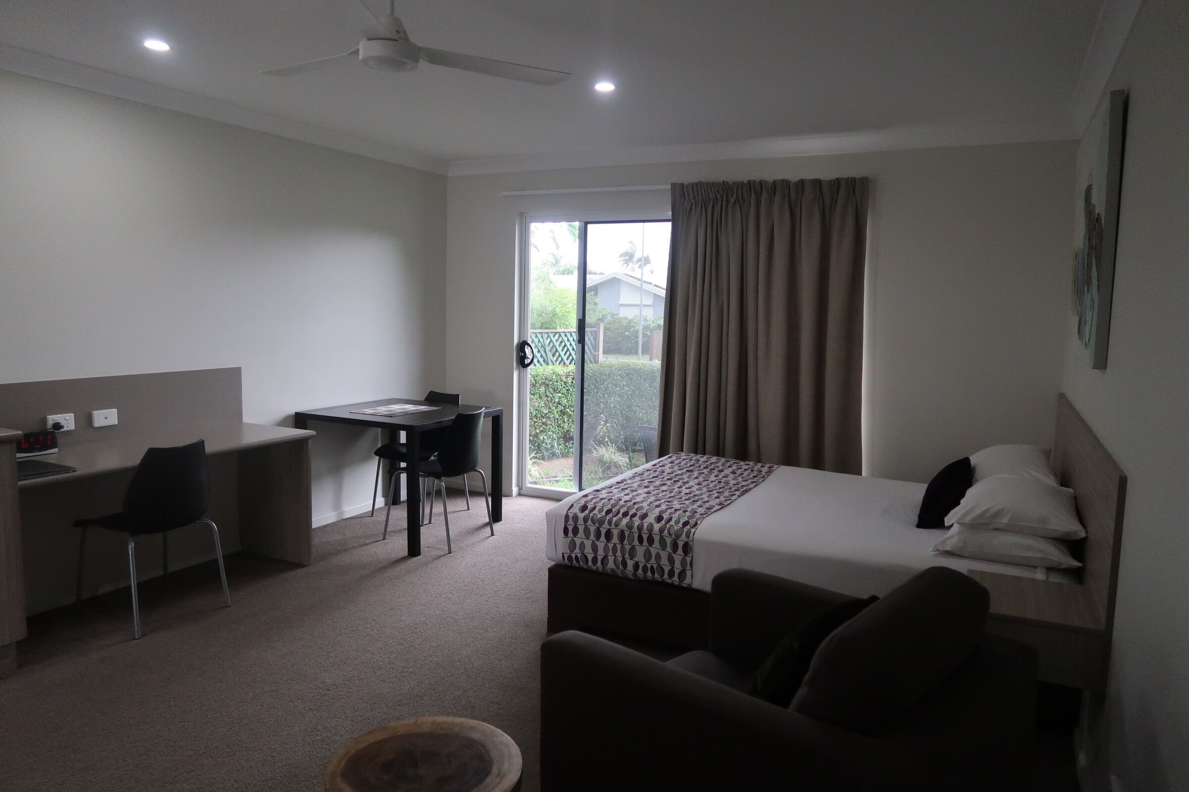 Quarto de hotel com cama, escrivaninha, cadeira e uma pequena mesa.