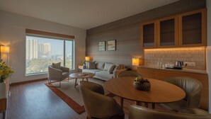 Uma sala de estar moderna com sofá, mesa de centro e área de jantar. Há uma janela grande com vista para edifícios.