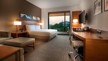 Quarto de hotel com uma cama, escrivaninha, poltrona, televisão e obras de arte na parede.