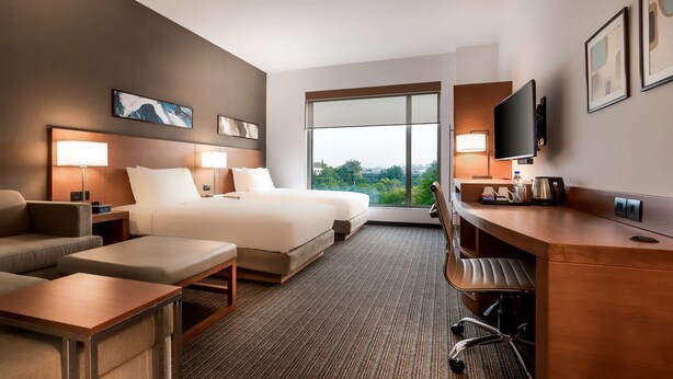 Quarto de hotel com uma cama, uma escrivaninha, uma cadeira, um sofá e uma televisão.