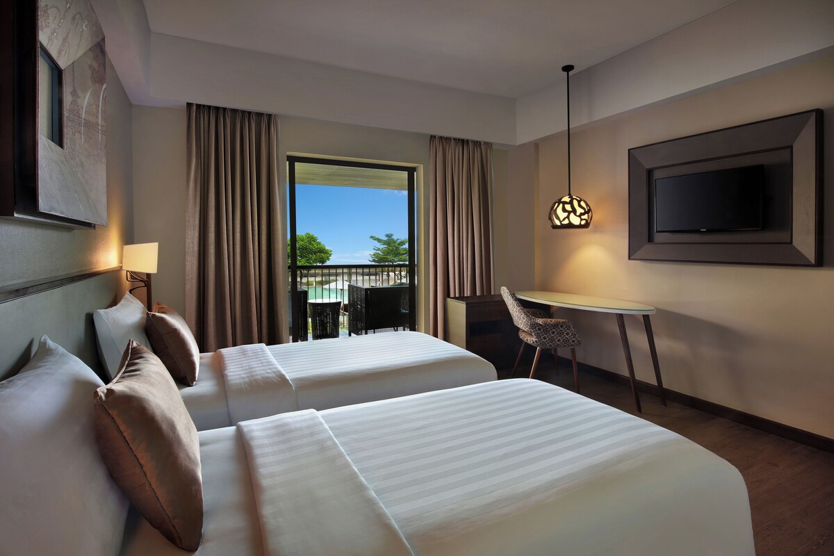 Quarto de hotel com duas camas, uma escrivaninha, televisão e varanda com vista.