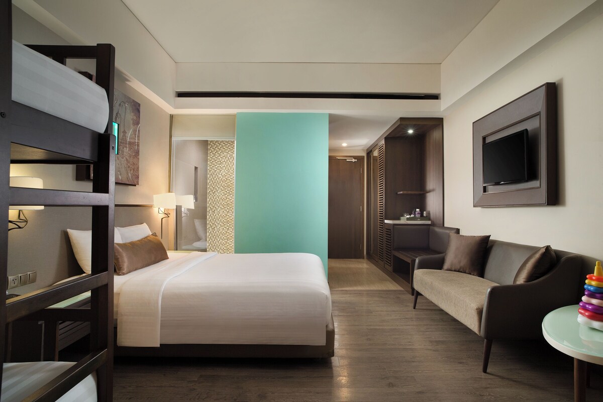 Quarto de hotel com cama, sofá, televisão e uma mesinha com brinquedos.