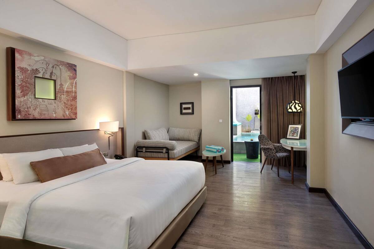 Quarto de hotel com uma cama grande, uma mesa de trabalho, uma cadeira, televisão e varanda com vista.