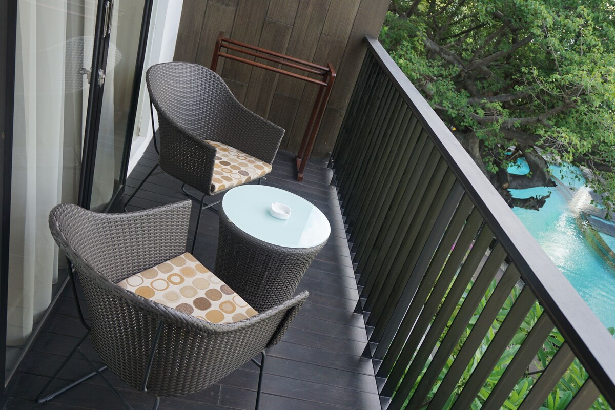 Varanda com mobiliário de vime, uma mesa pequena e vista para uma piscina.