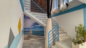Uma escadaria com corrimãos azuis, uma parede decorativa com um mural de um veleiro e um vaso de planta no patamar.