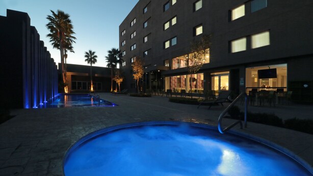 Um hotel com piscina, palmeiras e fachada de prédio moderna.