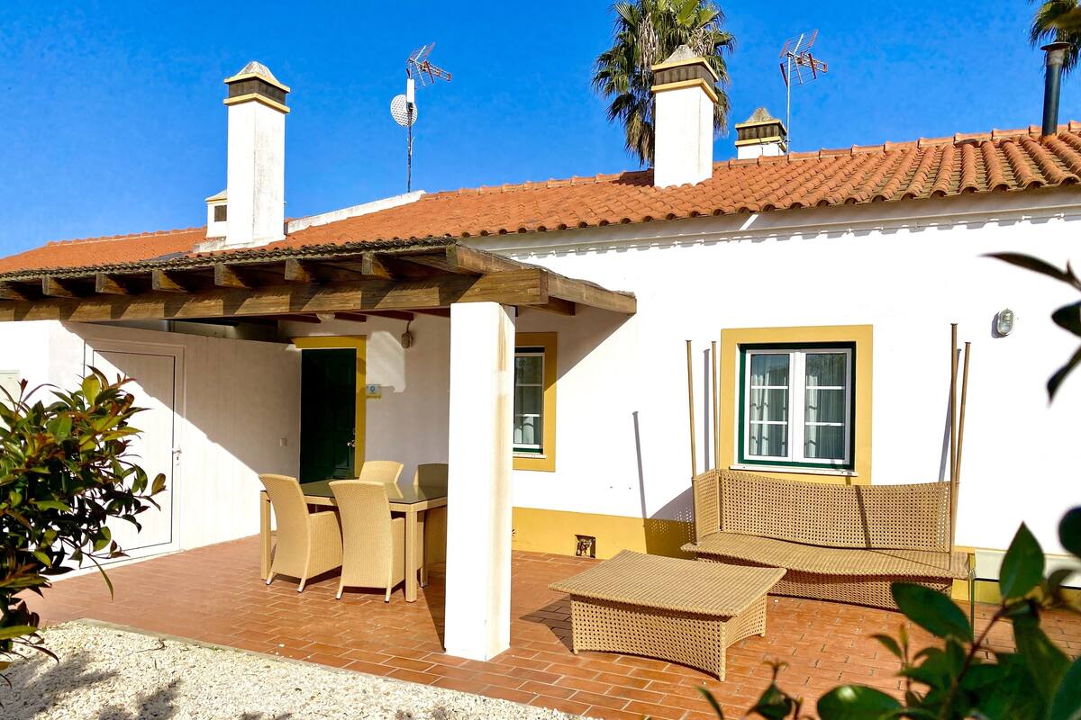 Uma casa com varanda, móveis de jardim e céu azul.