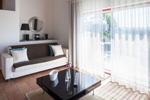 Uma sala de estar moderna com sofá, mesa de centro e uma janela grande com cortinas leves.