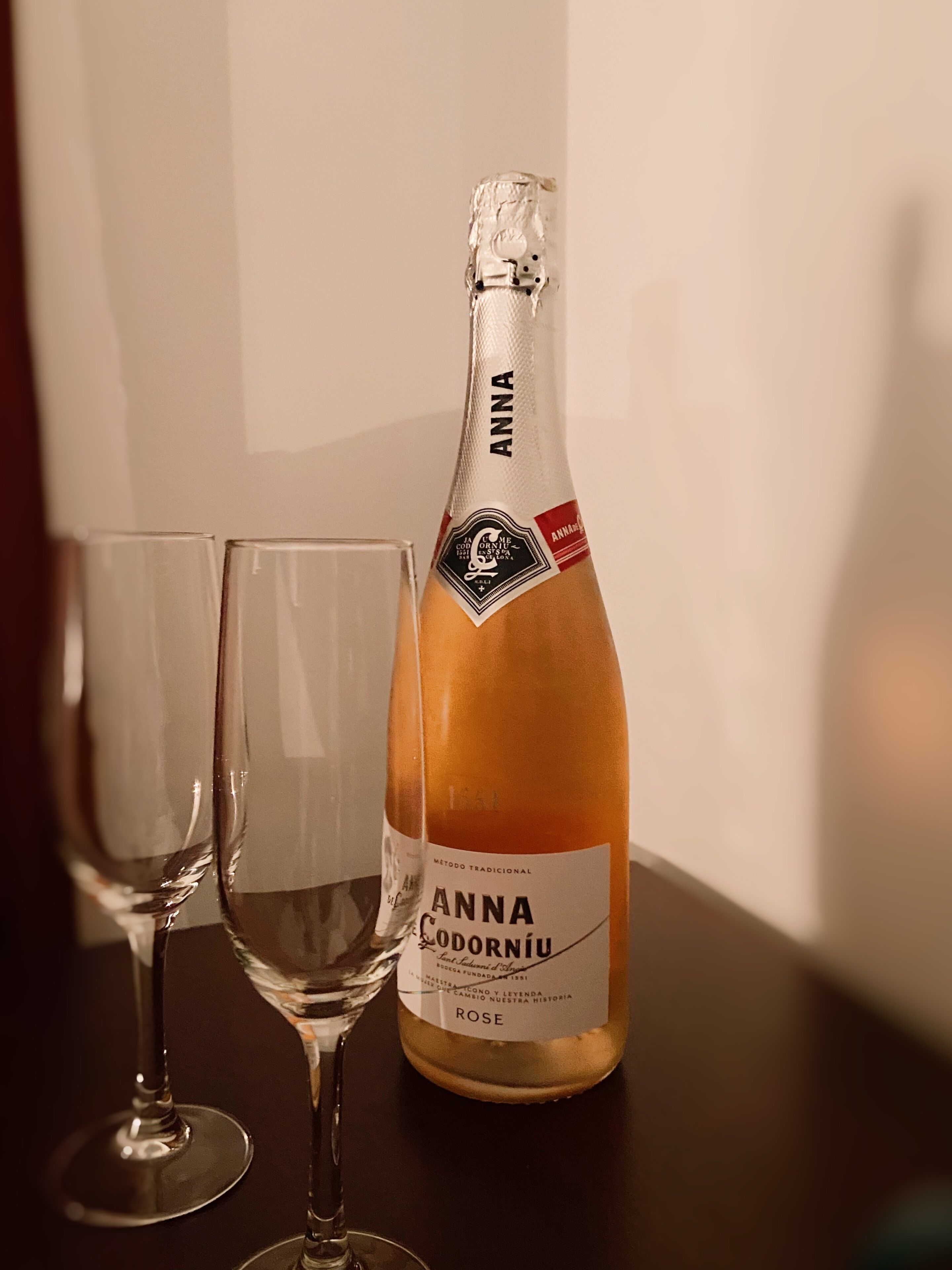Uma garrafa de champanhe rosé Anna Codorniu e dois copos de vinho vazios sobre uma mesa.