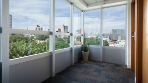 Quarto de canto com grandes janelas, um vaso de planta e piso coberto por carpete.