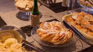 Uma mesa de buffet com diversos produtos de panificação, incluindo pães, doces e um bolo grande.