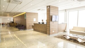 Uma área de recepção moderna, com um balcão de madeira, um sofá e uma tela de televisão.