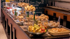 Buffet com diversas opções de comida, incluindo frutas, pão e doces.