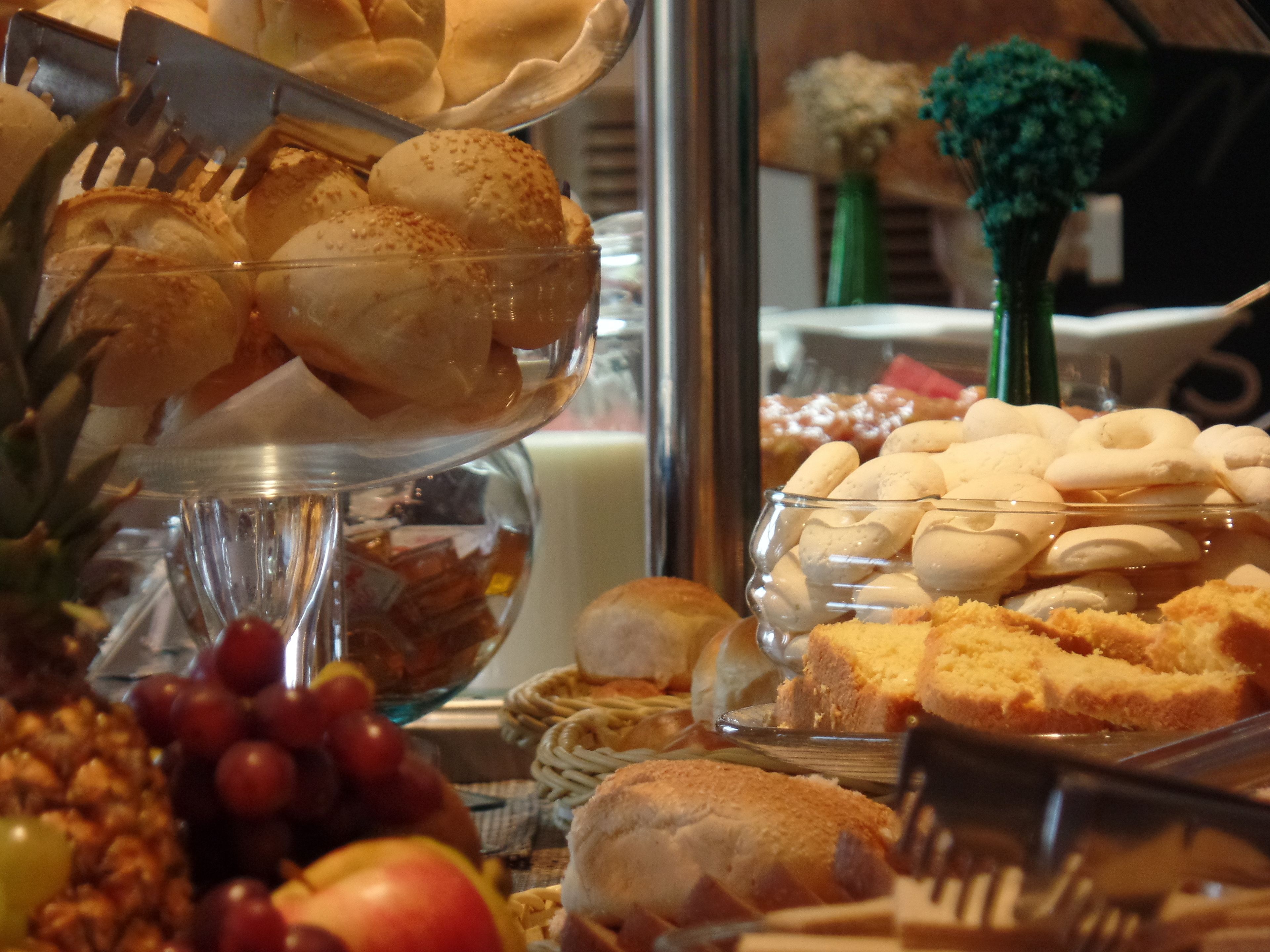 Buffet com diversos alimentos, incluindo pães, frutas e doces.