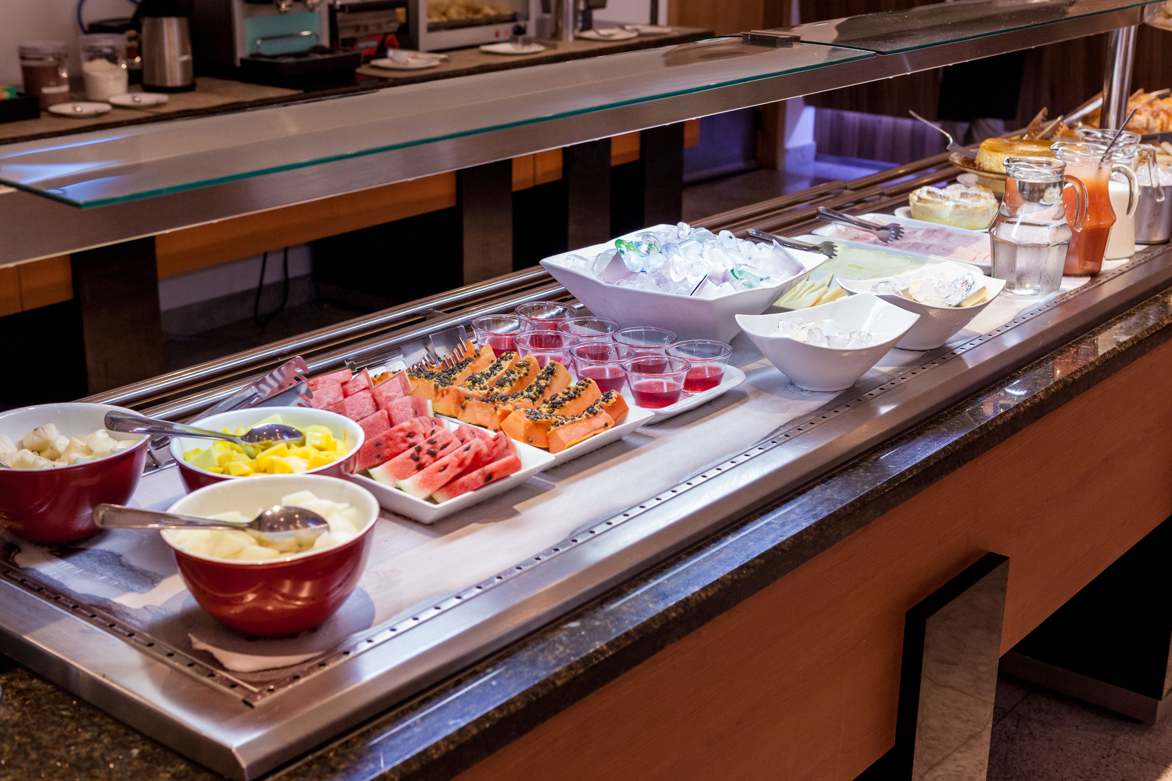 Buffet com diversos alimentos, incluindo frutas, legumes e sobremesas.