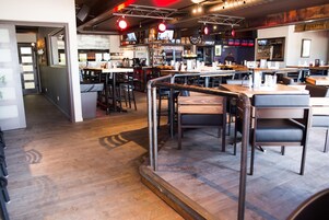 Restaurante com várias mesas e cadeiras, área de bar e sinalização visível para o banheiro.