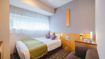 Quarto de hotel com cama, escrivaninha, cadeira e janela com cortinas leves.