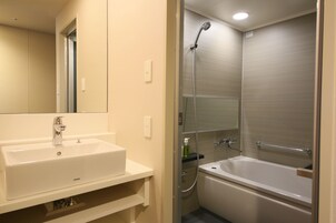 Uma casa de banho moderna com lavatório branco, espelho, chuveiro e banheira.