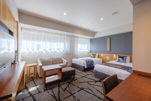 Quarto de hotel com cama, sofá, escrivaninha e televisão.