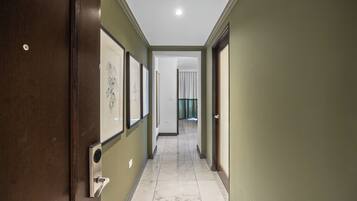 Um corredor com uma porta de madeira à esquerda, uma obra de arte emoldurada na parede e outra porta ao fundo.