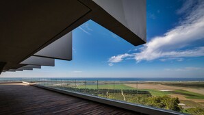Design arquitetônico moderno com uma ampla varanda de vidro e vista para a paisagem costeira.