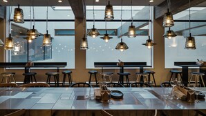 Um restaurante moderno com uma mesa comunitária grande, vários bancos altos e luminárias pendentes.