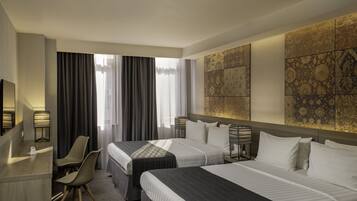 Quarto de hotel com duas camas, uma escrivaninha, uma cadeira e uma janela grande com cortinas.