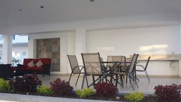 Uma área de refeições moderna ao ar livre, com mesa e cadeiras, um sofá vermelho e uma parede de pedra.