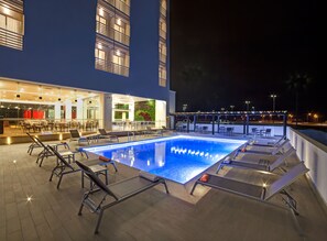 Área de piscina no terraço com espreguiçadeiras e um bar.